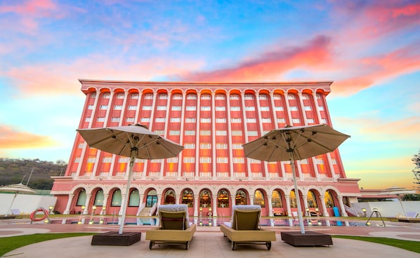 Um hotel com fachada grande e vermelha, várias varandas e área de estar ao ar livre com guarda-sóis.