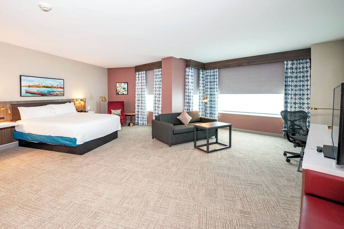 Quarto de hotel com cama, sofá, escrivaninha e cadeira.