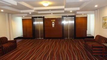 Um hall amplo com carpete estampado, dois elevadores e sofás listrados.