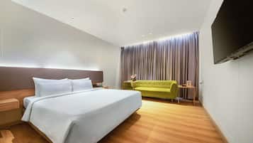 Quarto de hotel moderno com uma cama grande, um sofá verde, uma televisão de tela plana e piso de madeira.