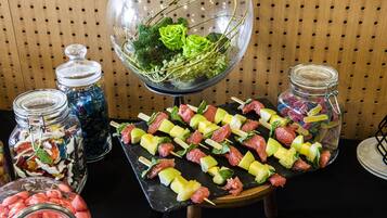 Exposição de comida com espetos de frutas e legumes, e potes com vários tipos de doces.
