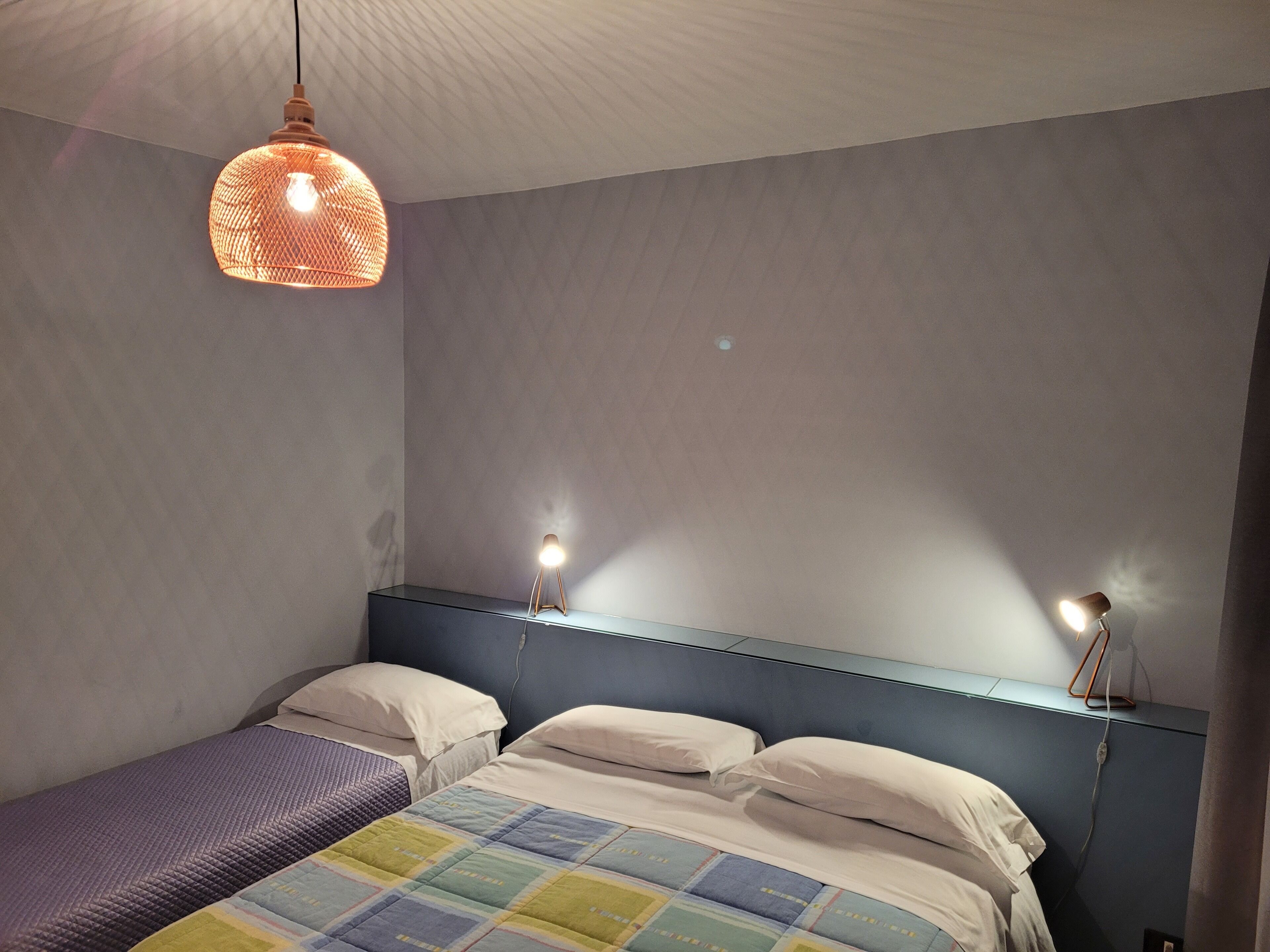 Quarto com cama, cabeceira e luminária pendente.