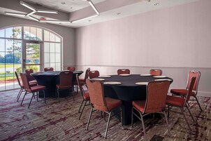 Uma sala de conferências com uma mesa grande e cadeiras, janelas amplas e piso coberto por carpete.