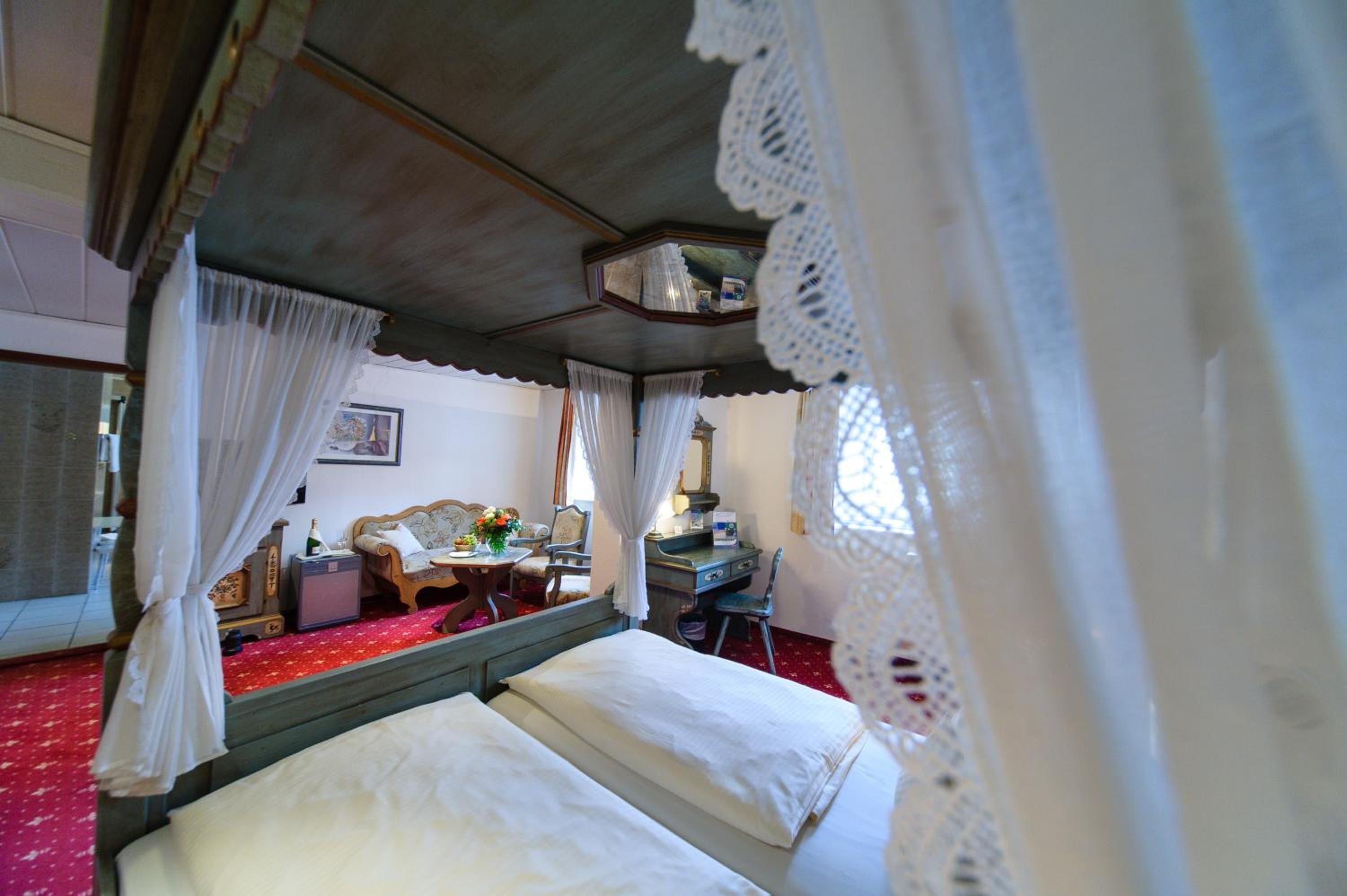 Quarto com cama, escrivaninha e cadeira. Há uma janela com cortinas.