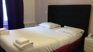 Cama bem arrumada com lençóis e almofadas brancos, cabeceira escura e uma pequena mesa de cabeceira com um telefone.