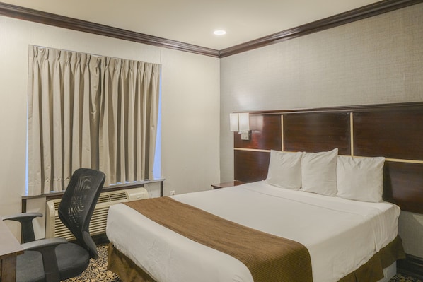 Quarto de hotel com uma cama grande, uma escrivaninha com cadeira e uma janela com cortinas.