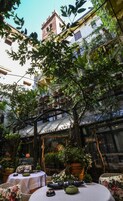 Um pátio com pérgola de vidro, mesas com toalhas de mesa florais e plantas em vasos.