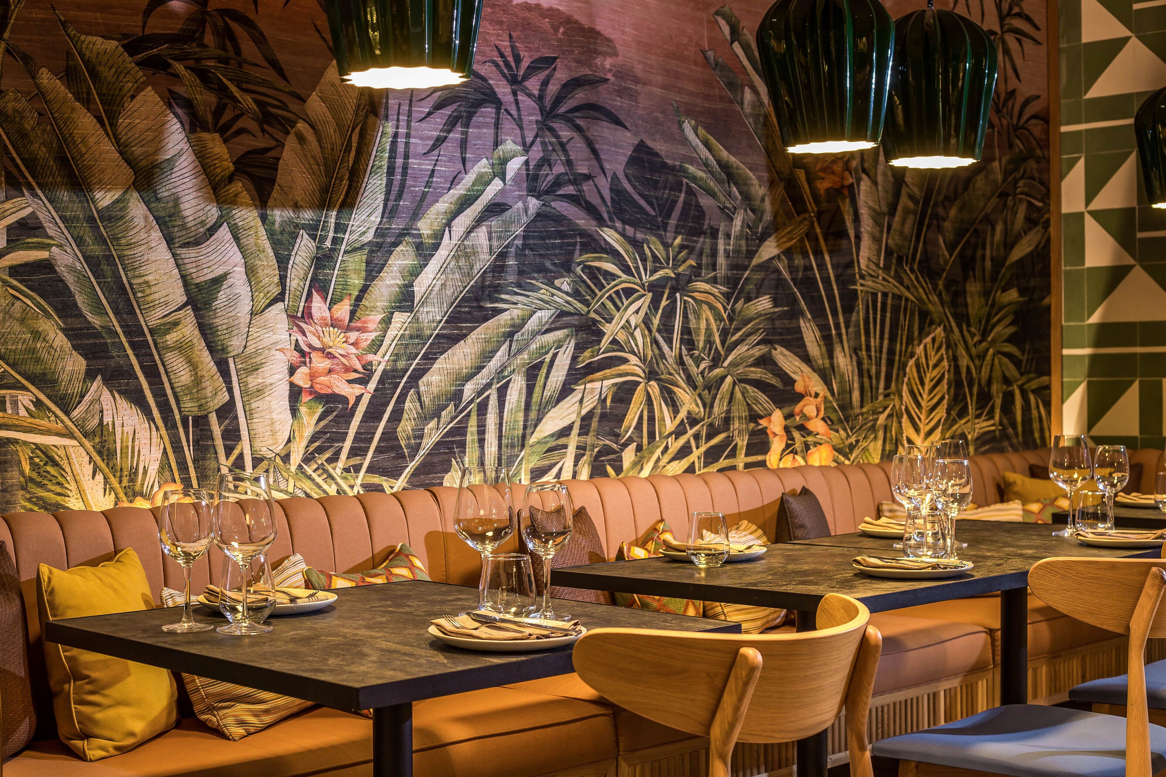 Restaurante com mural tropical, móveis de madeira e luminárias pendentes verdes.