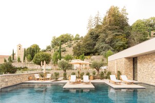 Piscina com espreguiçadeiras e guarda-sóis, cercada por muros de pedra e vegetação.