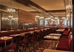 Um restaurante com assentos estofados vermelhos, mesas de madeira e lustres.