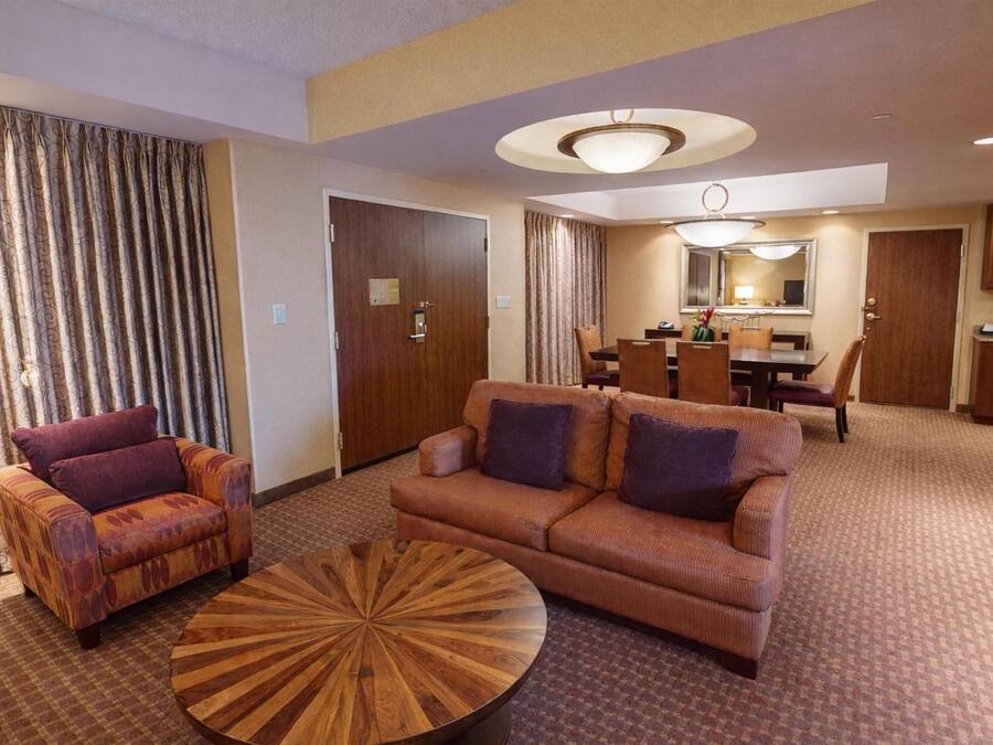 Quarto de hotel com sofá, poltrona, mesa de jantar e mesa de centro redonda.