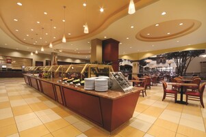 Uma área de buffet com ilha central, diversos arranjos de assentos e teto com iluminação embutida.