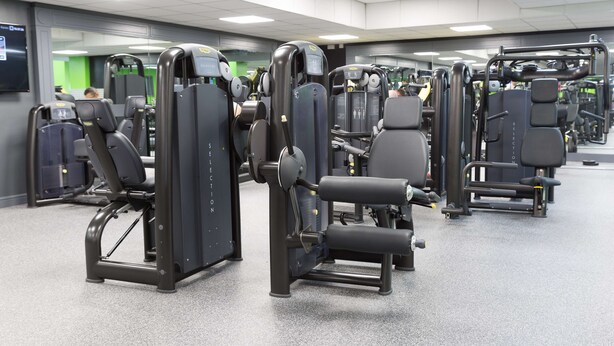 Uma academia com diversos aparelhos de ginástica, incluindo aparelhos de musculação e equipamentos de cardio.