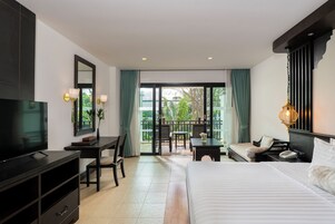 Quarto de hotel com cama, escrivaninha, televisão e varanda com vista para o verde.