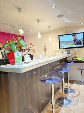Uma área de bar com banquetas, uma tela de televisão e plantas decorativas.