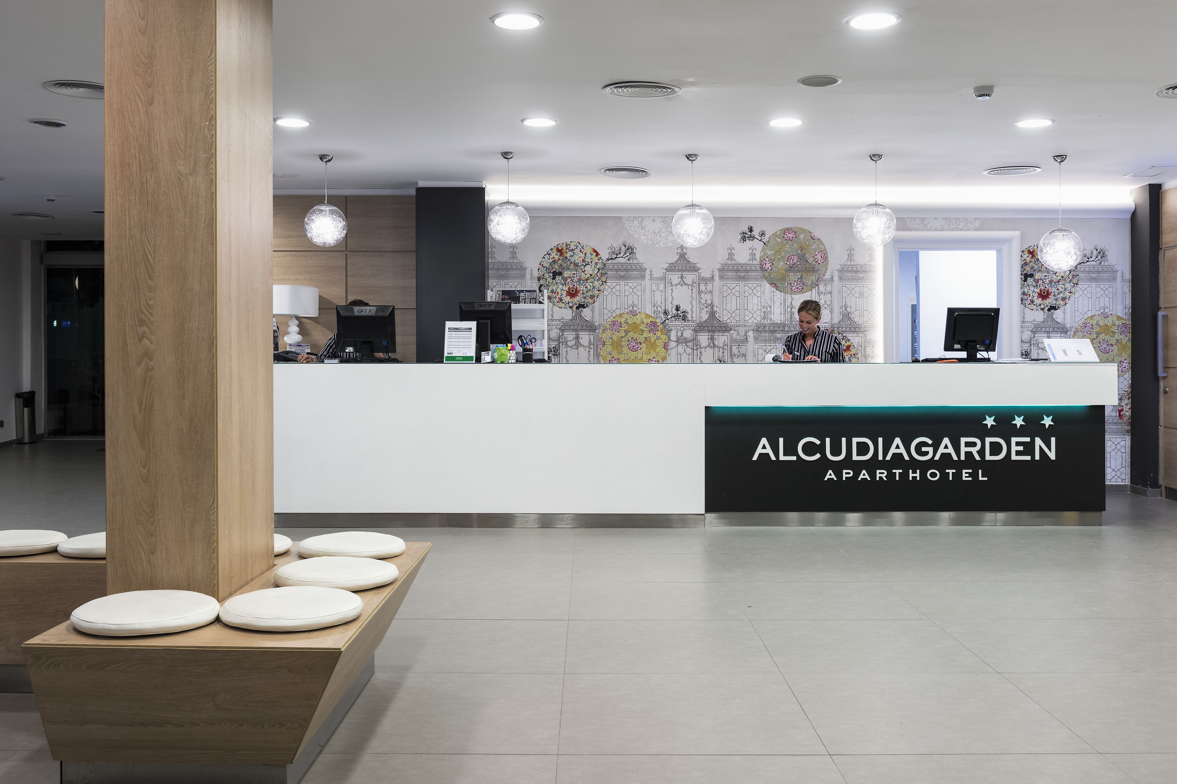 Uma área de recepção com design moderno, com um balcão de atendimento, um pilar de madeira e um espaço de estar com banquetas redondas.