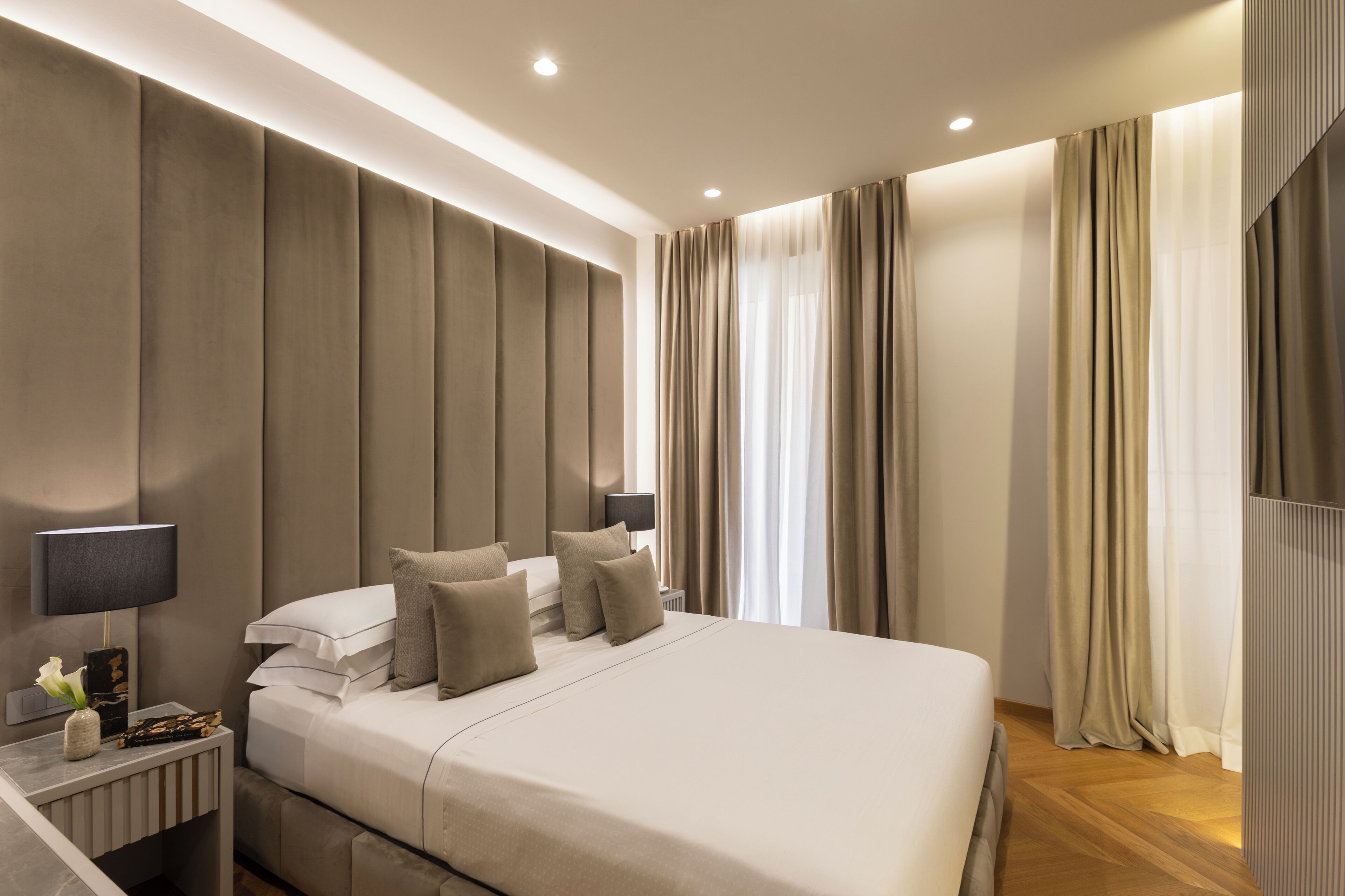 Quarto de hotel moderno com uma cama grande, mesas de cabeceira, luminária e cortinas.