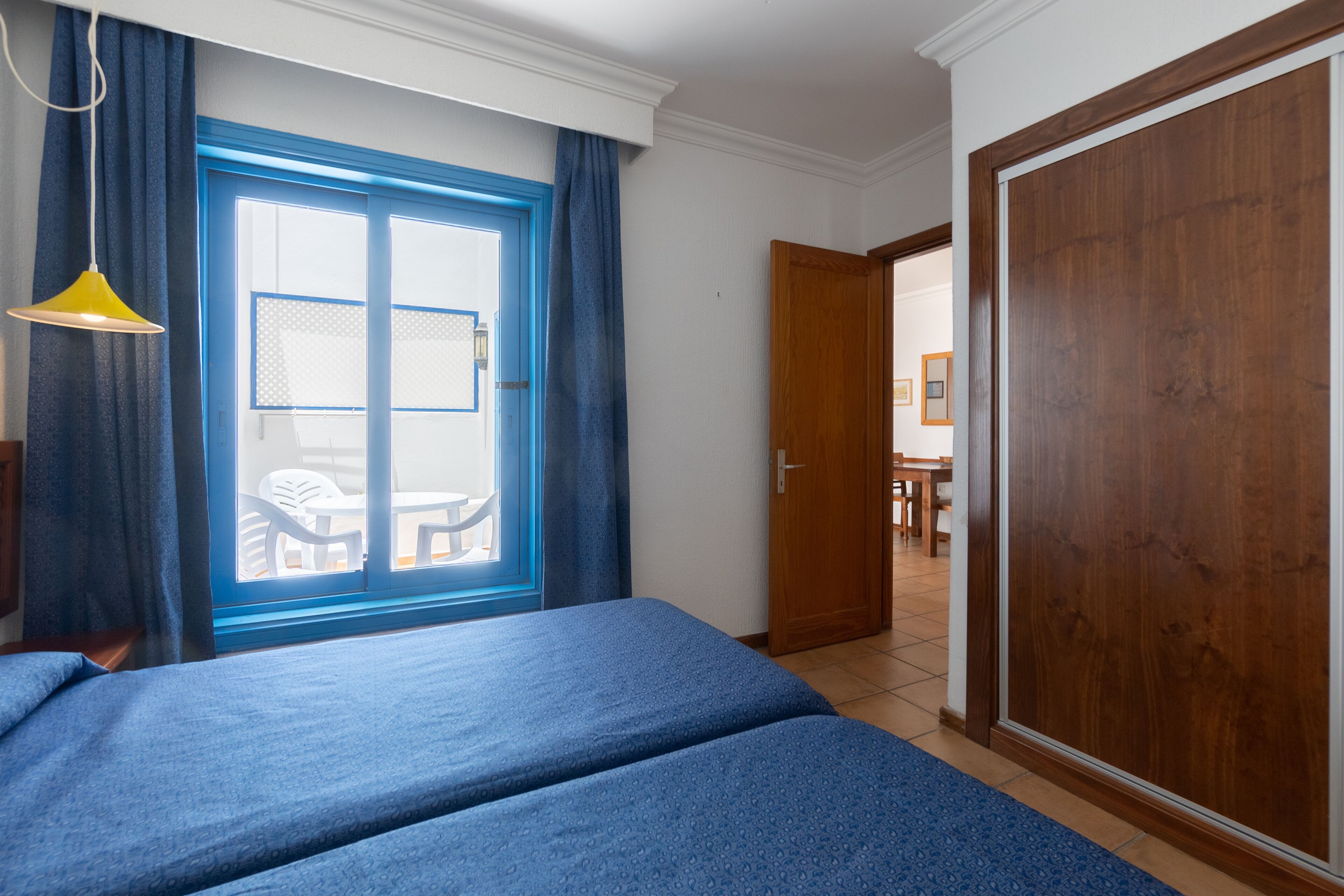 Quarto com uma cama grande, janela com cortinas azuis e um guarda-roupa de madeira.