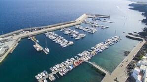Vista aérea de um porto com diversos barcos atracados, um cais e uma paisagem costeira.