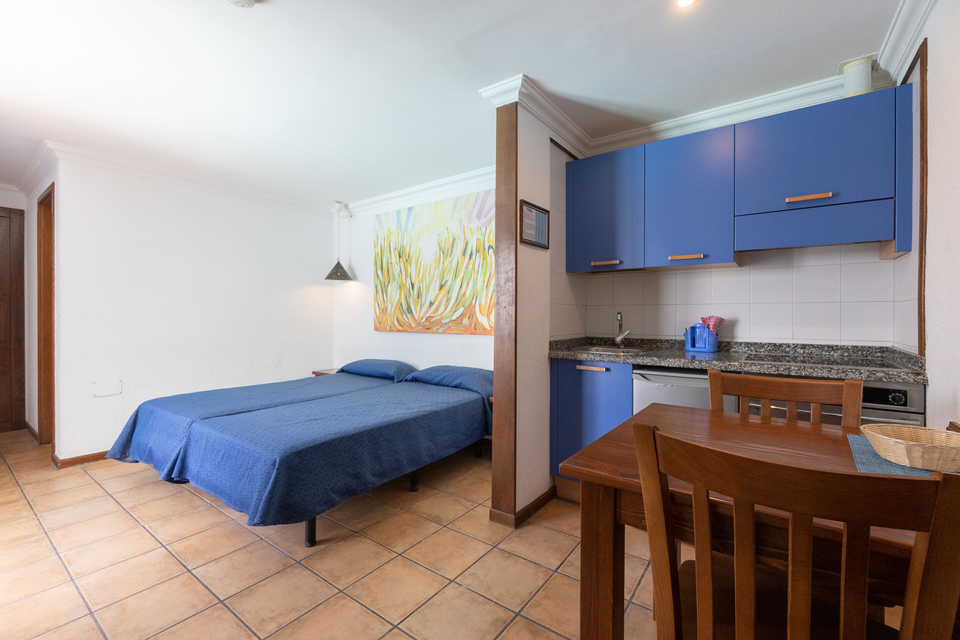 Quarto compacto com uma cama, uma mesa pequena e uma cozinha compacta.