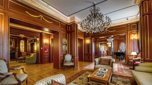 Um hall imponente com painéis de madeira, um candelabro e móveis clássicos.