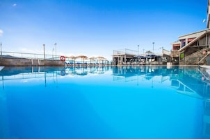Piscina azul límpida com espreguiçadeiras e guarda-sóis, um flutuador e um edifício com varanda.