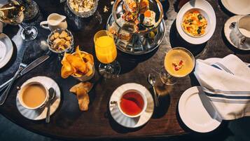 Mesa de jantar posta com diversos pratos, incluindo um suporte de servir em três níveis, tigelas e copos.