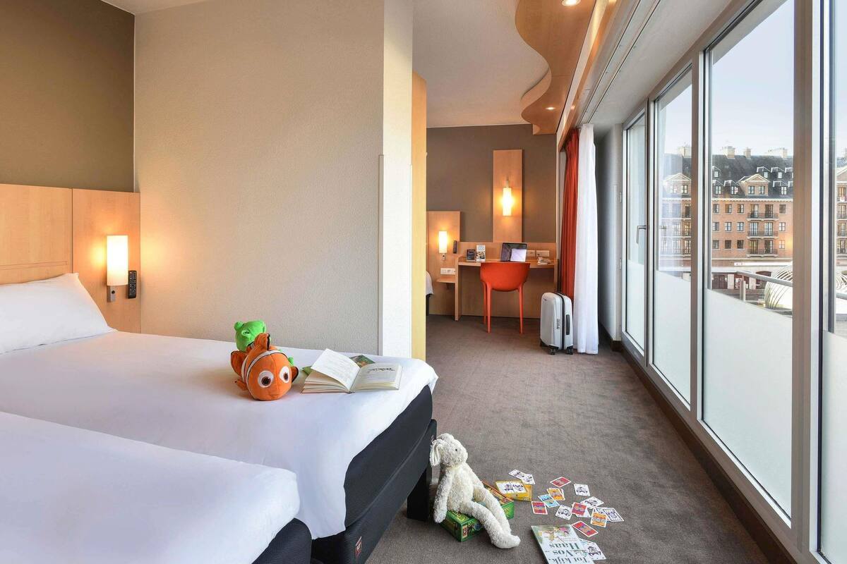 Quarto de hotel com cama, escrivaninha, cadeira e vista da cidade.