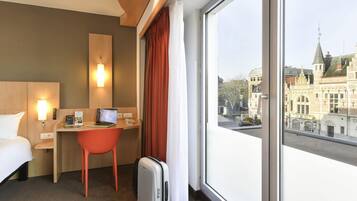 Quarto de hotel com cama, escrivaninha, cadeira, laptop e mala.