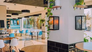 Uma área de refeições moderna com mesas redondas, cadeiras azuis e luminárias pendentes pretas.