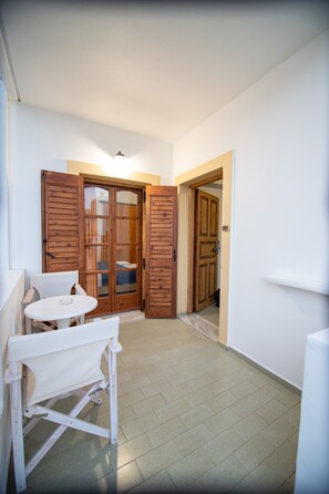 Um corredor com piso de azulejos brancos, uma mesa branca com cadeiras e portas de madeira.