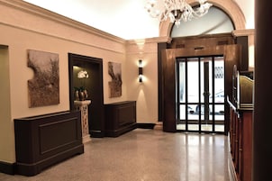 Um hall de hotel com entrada imponente, obras de arte nas paredes e um lustre.
