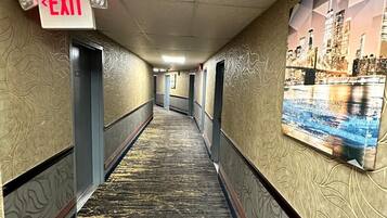 Corredor de hotel com paredes estampadas, placa de saída e um mural com vista para a cidade.