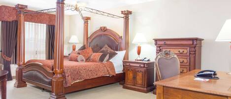 Uma cama de dossel com estrutura de madeira e toldo, uma escrivaninha de madeira com telefone e uma cadeira.