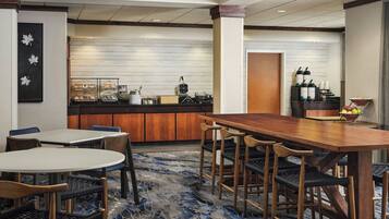 Uma sala de jantar de hotel com uma longa mesa de madeira e cadeiras, um balcão de buffet e um resfriador de vinhos fixado na parede.