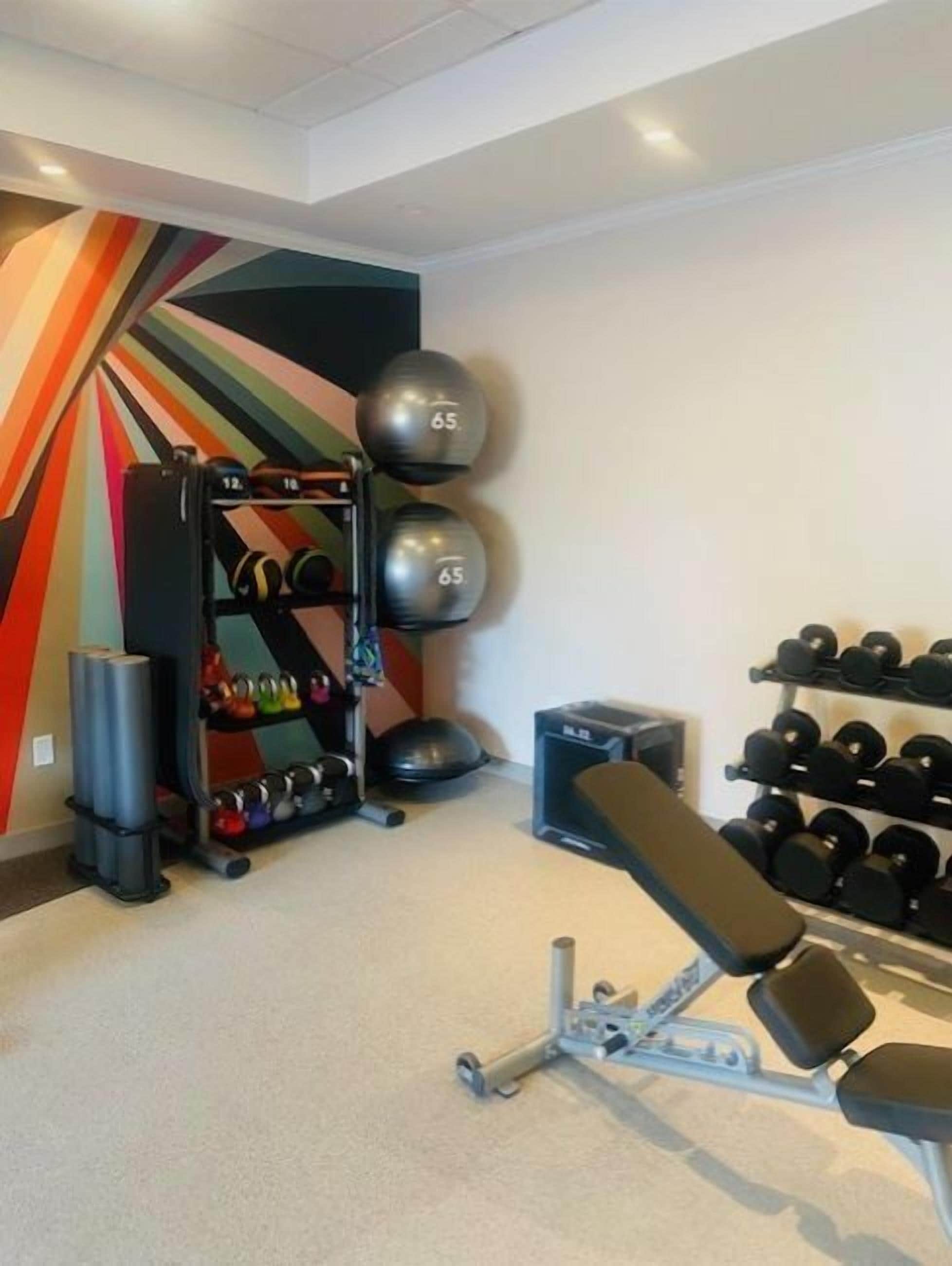 Uma academia com equipamentos de musculação, um banco e uma parede colorida.