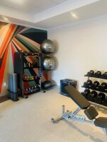 Uma academia com equipamentos de musculação, um banco e uma parede colorida.