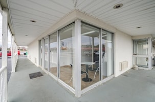 Área externa coberta com portas de vidro que dão para um espaço interno, uma pequena mesa com cadeiras e vista para a rua.