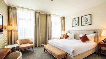 Quarto de hotel com uma cama grande, uma cadeira, um banco, uma escrivaninha e uma televisão.
