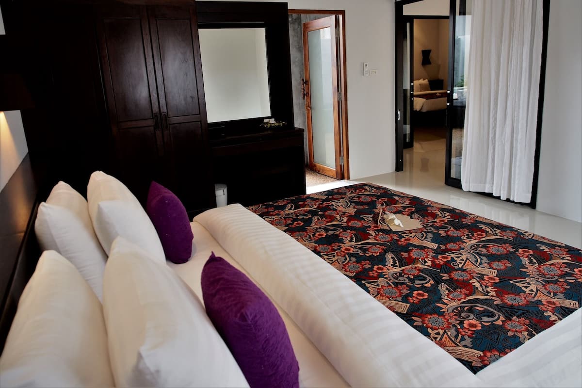Um quarto com uma cama, um guarda-roupa de madeira escura, um espelho grande e um tapete estampado.