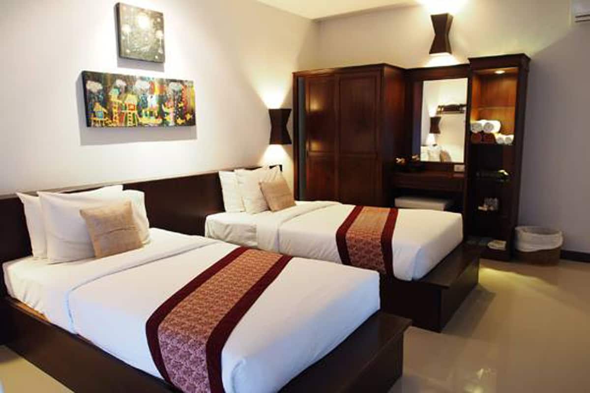 Quarto de hotel com duas camas, um guarda-roupa, um espelho e obras de arte na parede.