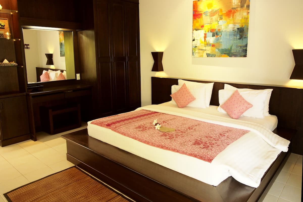 Quarto de hotel moderno com uma cama grande, um guarda-roupa de madeira escura, um espelho e uma pintura abstrata colorida na parede.