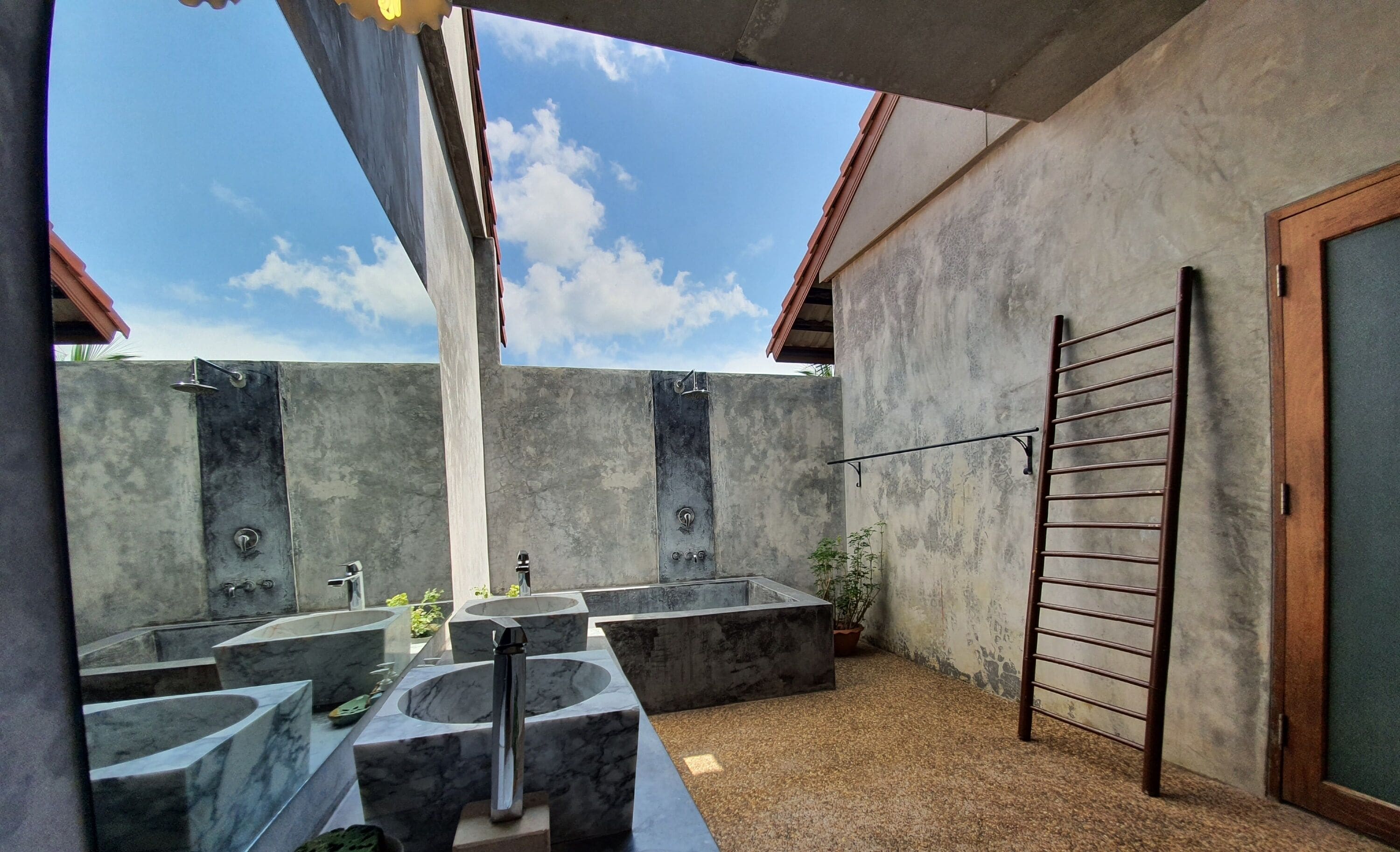 Um banheiro ao ar livre moderno, com várias pias de mármore e área de chuveiro em concreto.