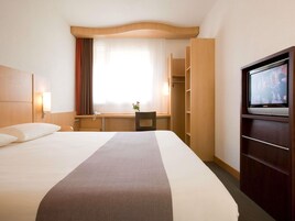 Quarto de hotel com cama, escrivaninha, televisão e armário.