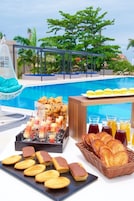Disposição de café da manhã à beira da piscina, com pães, sanduíches e bebidas.