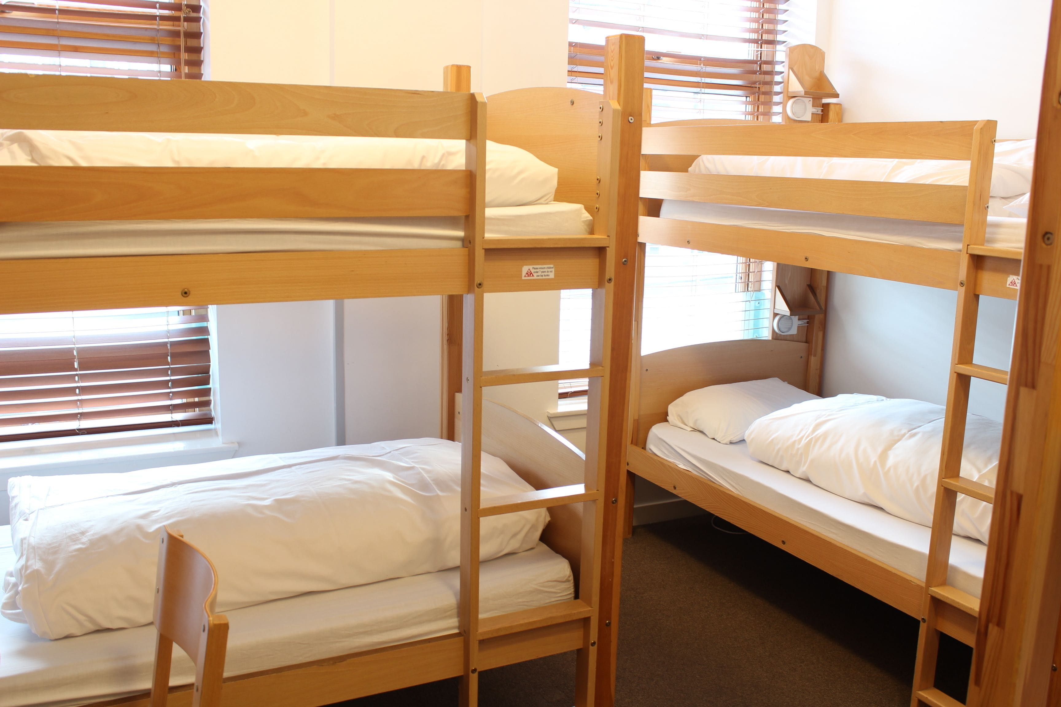 Quarto com beliches de três andares, estrutura de madeira e roupa de cama branca.