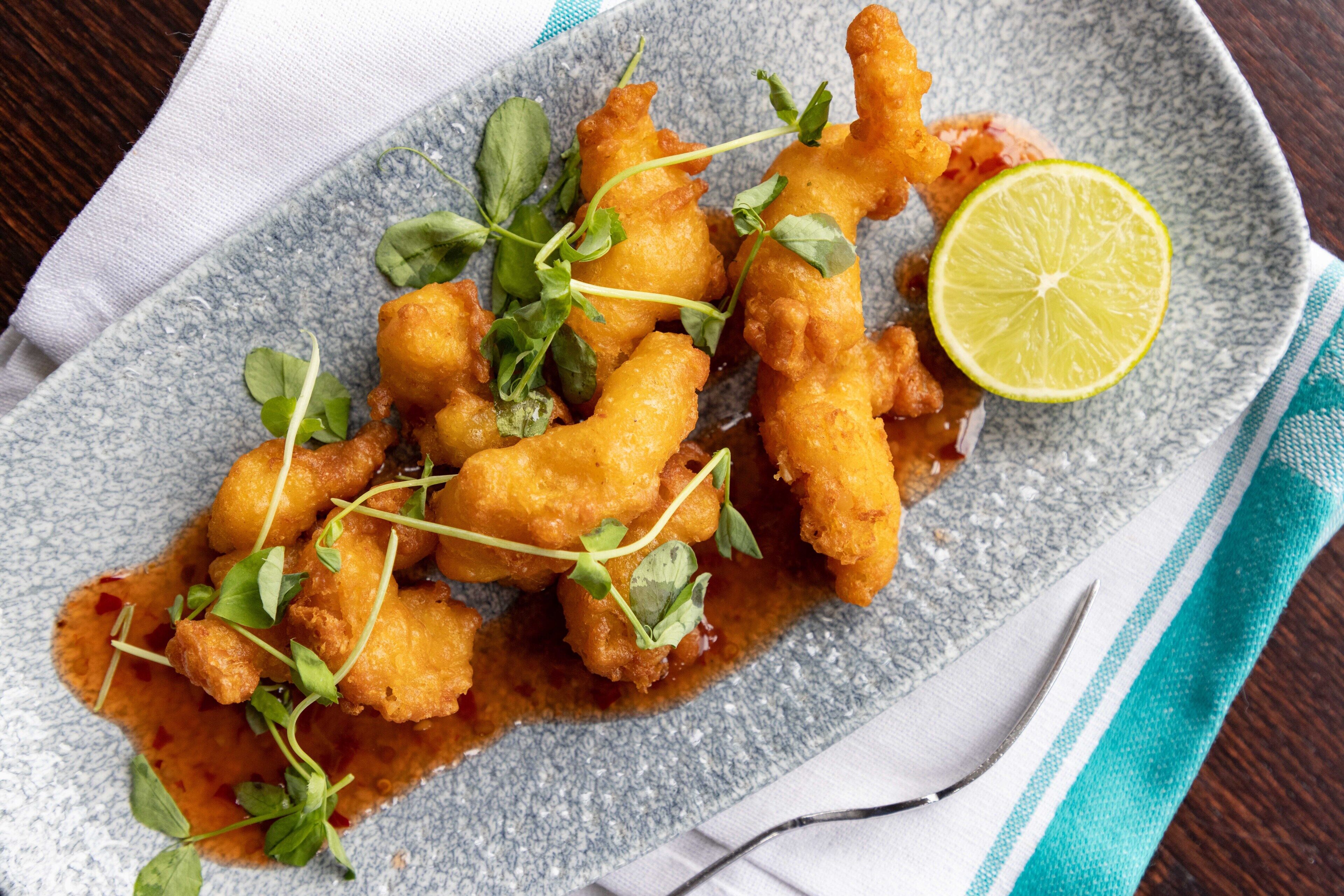 Prato de comida frita crocante, decorado com folhas verdes e uma fatia de limão.