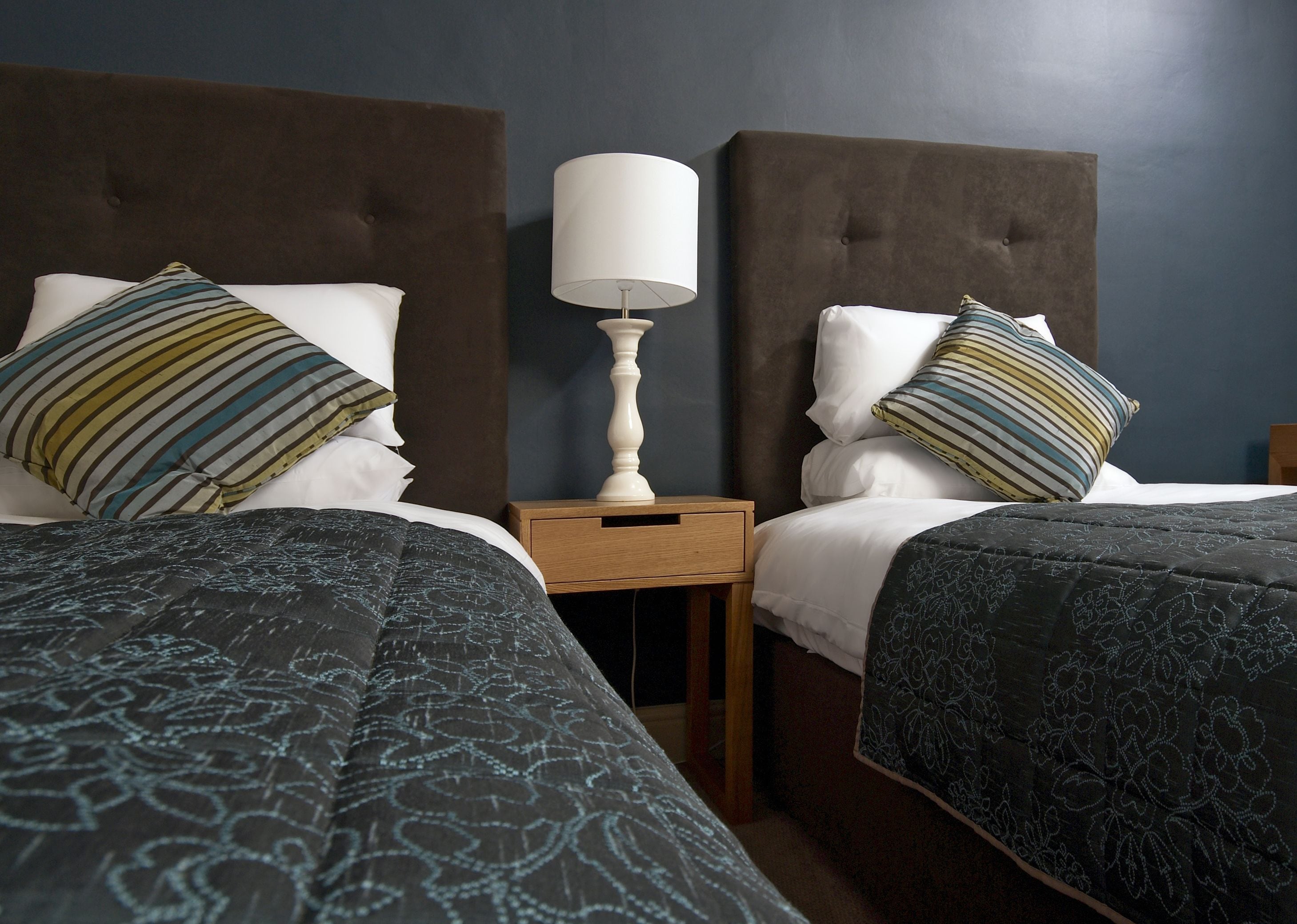 Quarto de hotel com duas camas, cada uma com cabeceira, mesa de cabeceira e almofadas listradas.