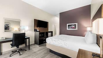 Quarto de hotel com cama, escrivaninha, cadeira, televisão e uma pequena mesa.