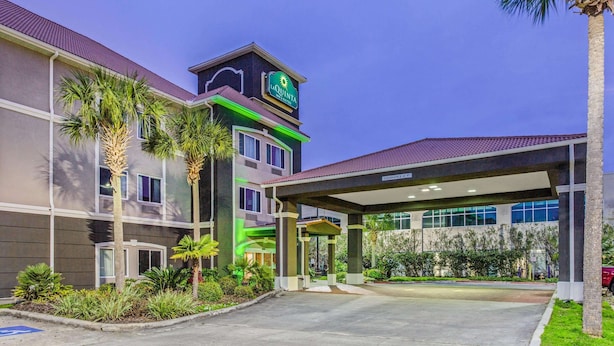 Hotel com design moderno, apresentando uma placa 'La Quinta' em destaque, área de estacionamento coberta e paisagismo exuberante.